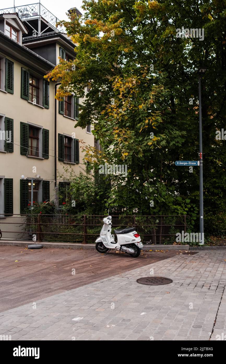 A Vertical shot of a white Vespa scooter in the street with trees in ...