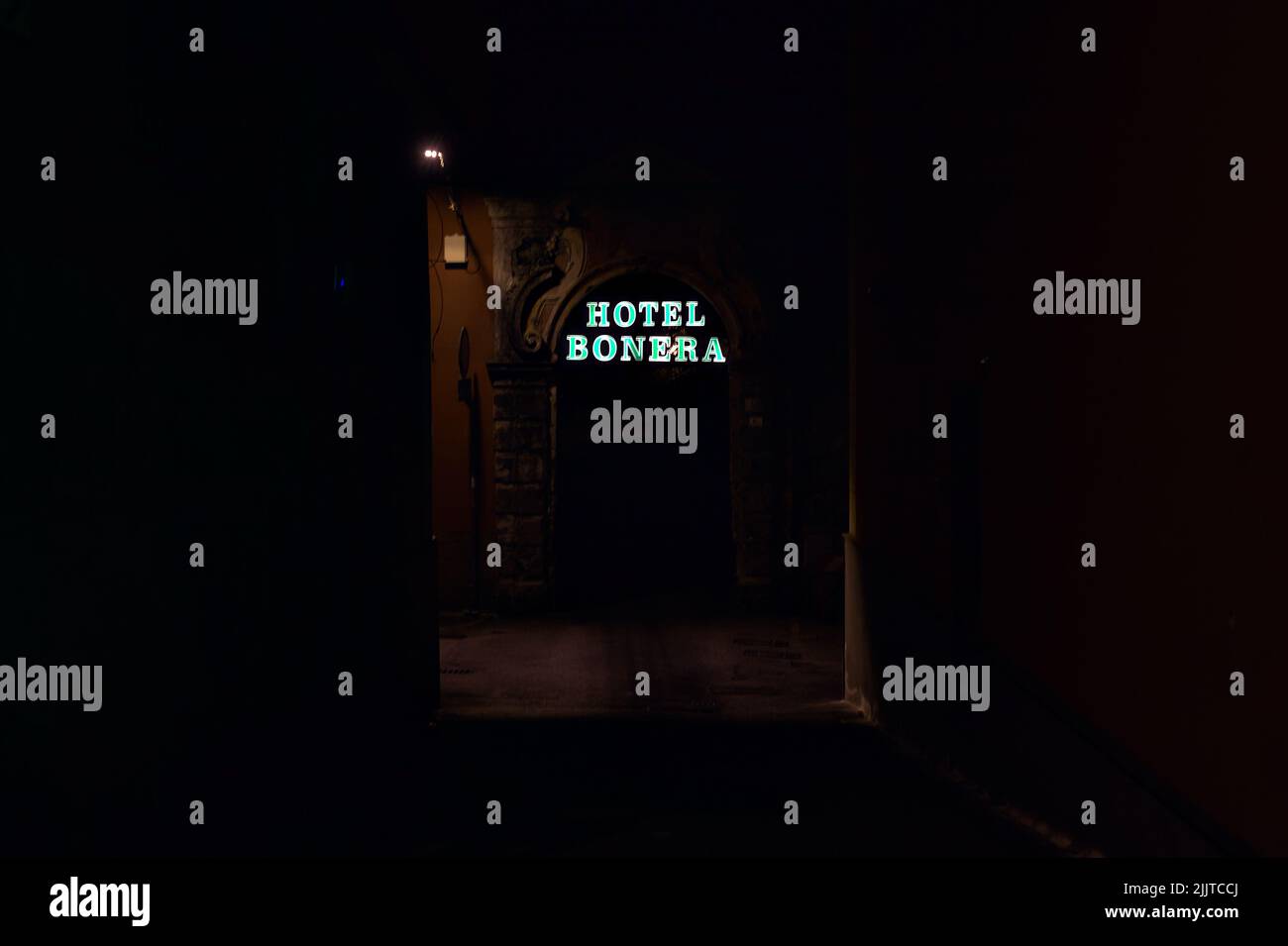 Access alley to a hotel with glowing sign lit by a dim street light at ...