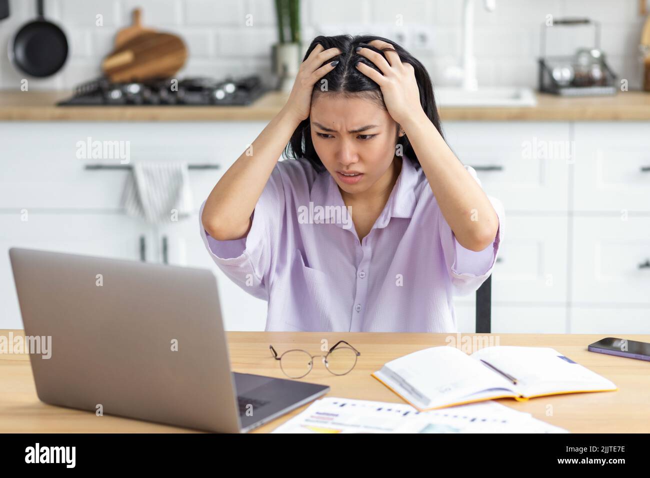 Young woman freelancer looking worried at laptop screen holding her ...