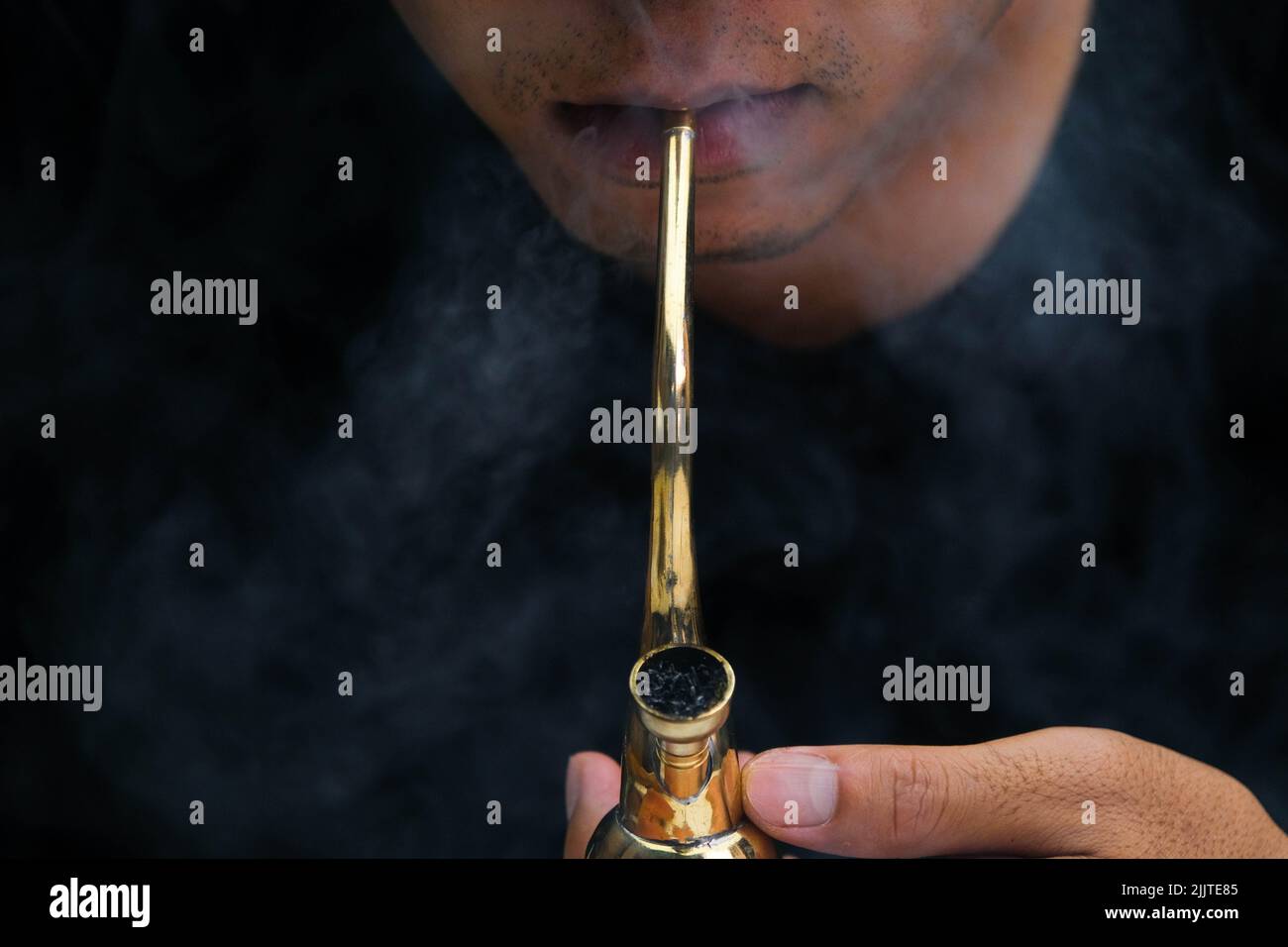 Asian man smokes marijuana from a pipe at home. Studio shoot with model ...