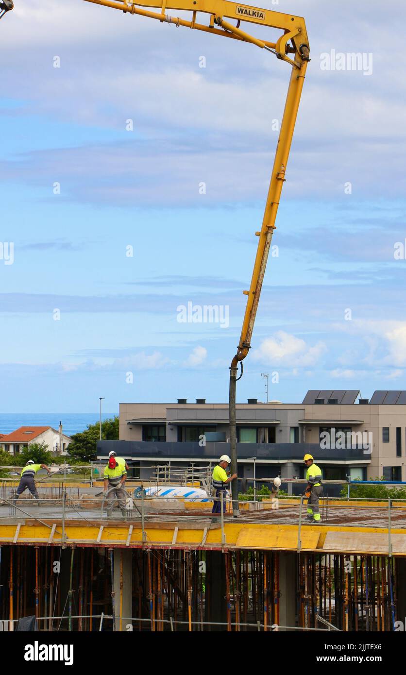 Construction workers comb newly poured concrete from a boom arm pumped ...