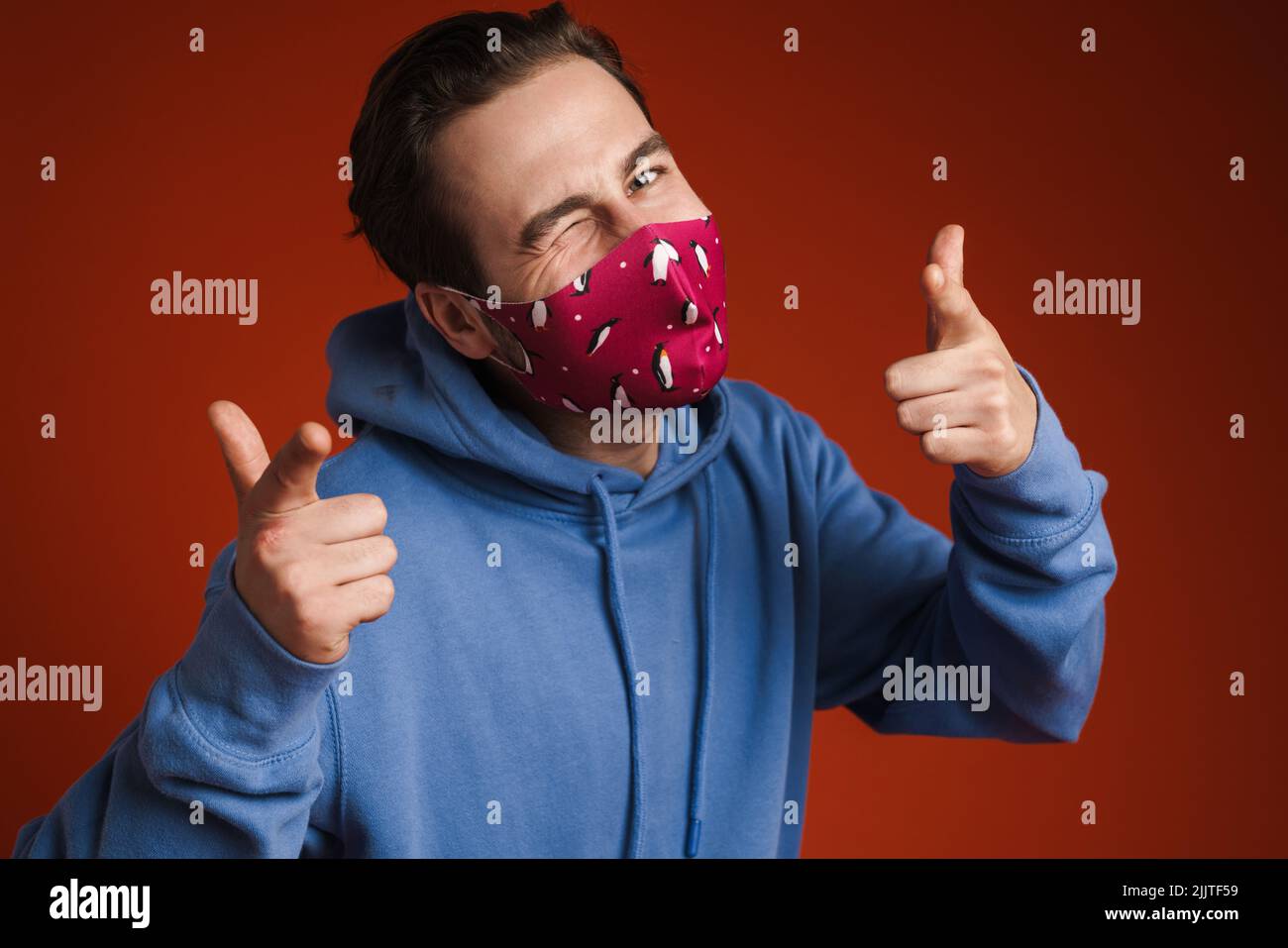 Young man wearing face mask winking and pointing fingers at camera ...