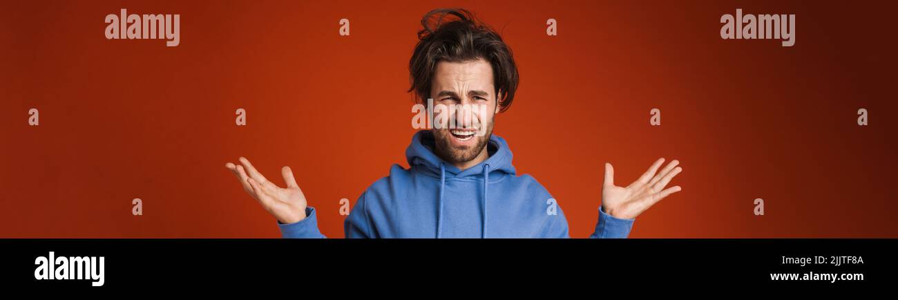 Young disheveled man grimacing and gesturing at camera isolated over ...