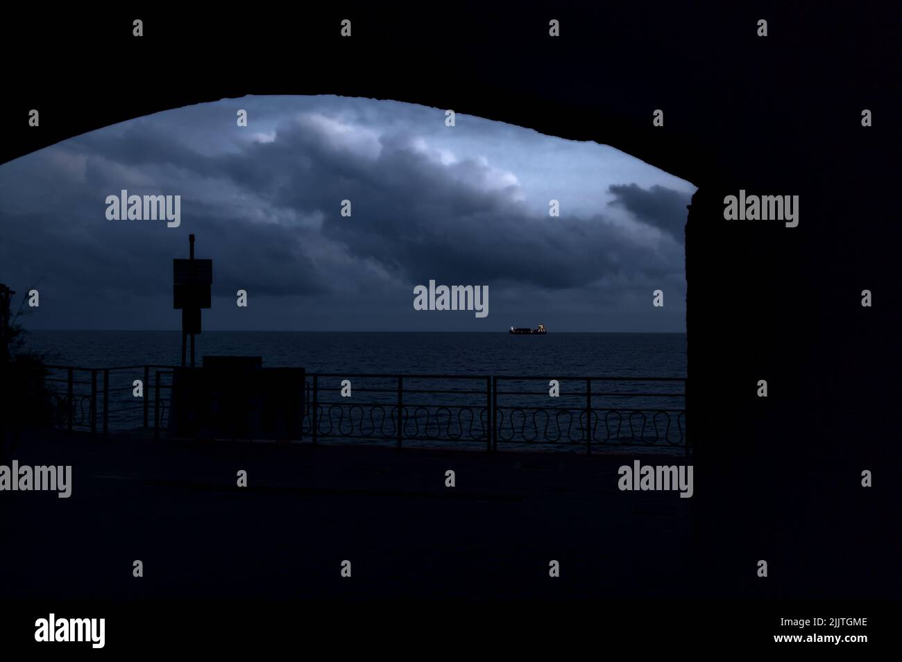 Sea at dusk with a cargo ship in the distance framed by an arch Stock ...