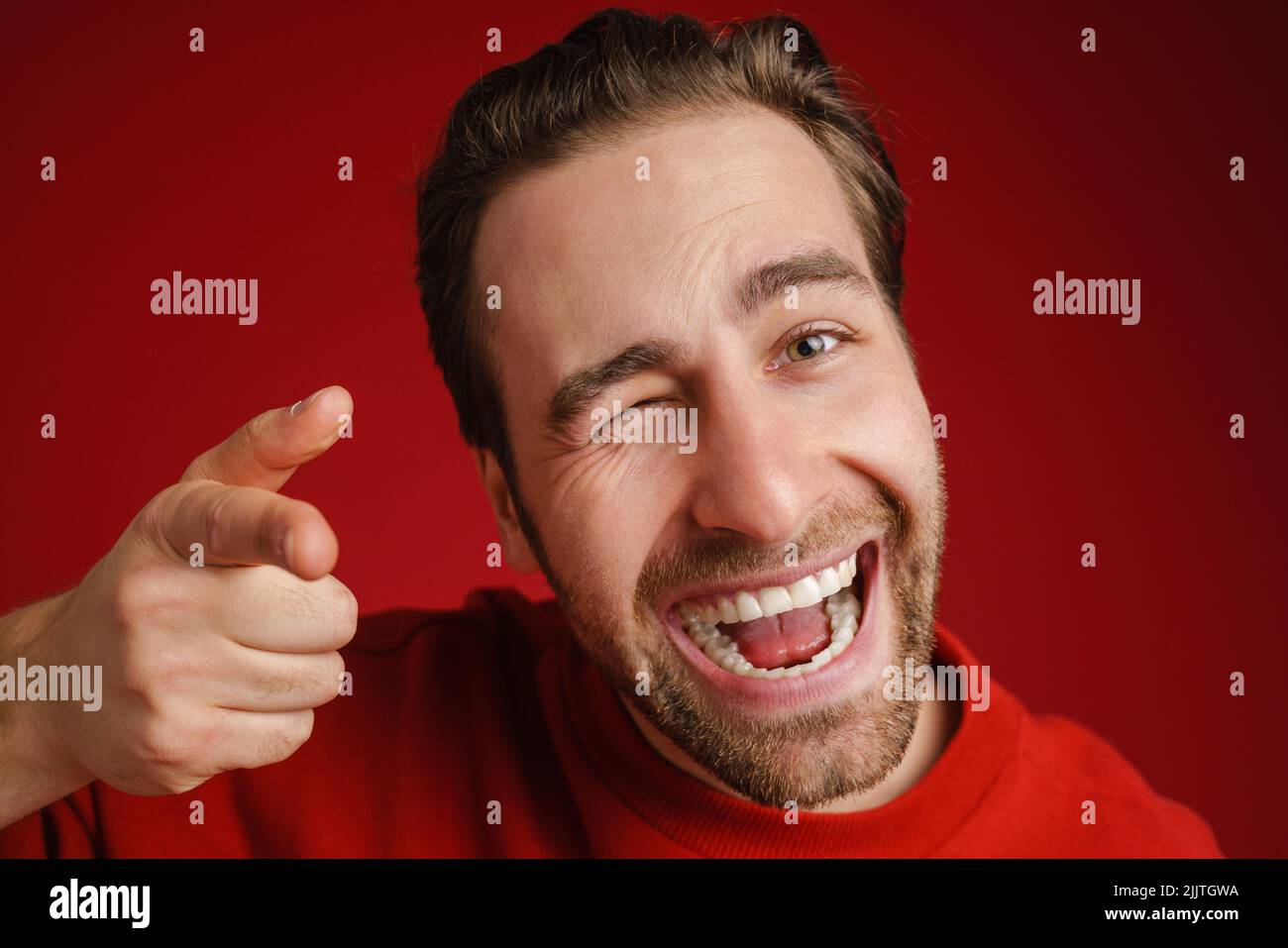 Young bristle man winking and pointing finger at camera isolated over ...