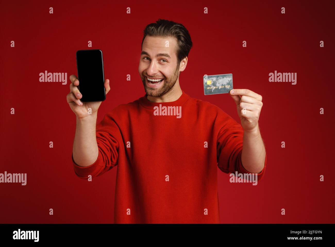Surprised man smiling while showing credit card and cellphone isolated ...
