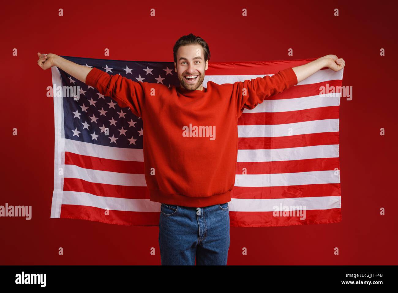 Young bristle man smiling while posing american flag isolated over red ...