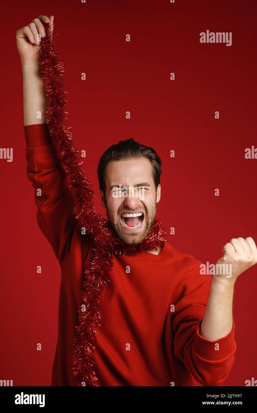 Young bristle man with tinsel screaming while making winner gesture ...