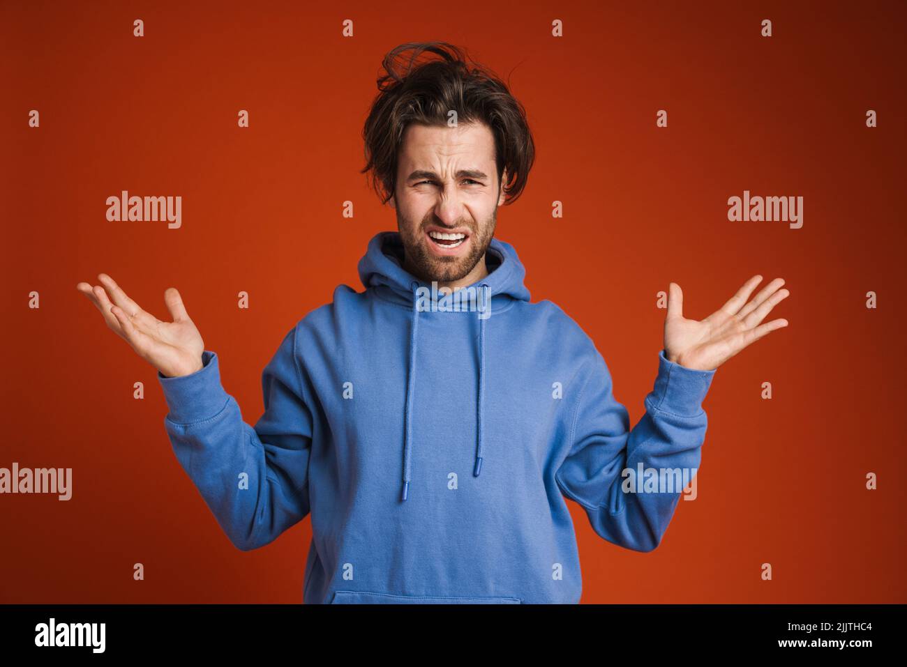 Young disheveled man grimacing and gesturing at camera isolated over ...