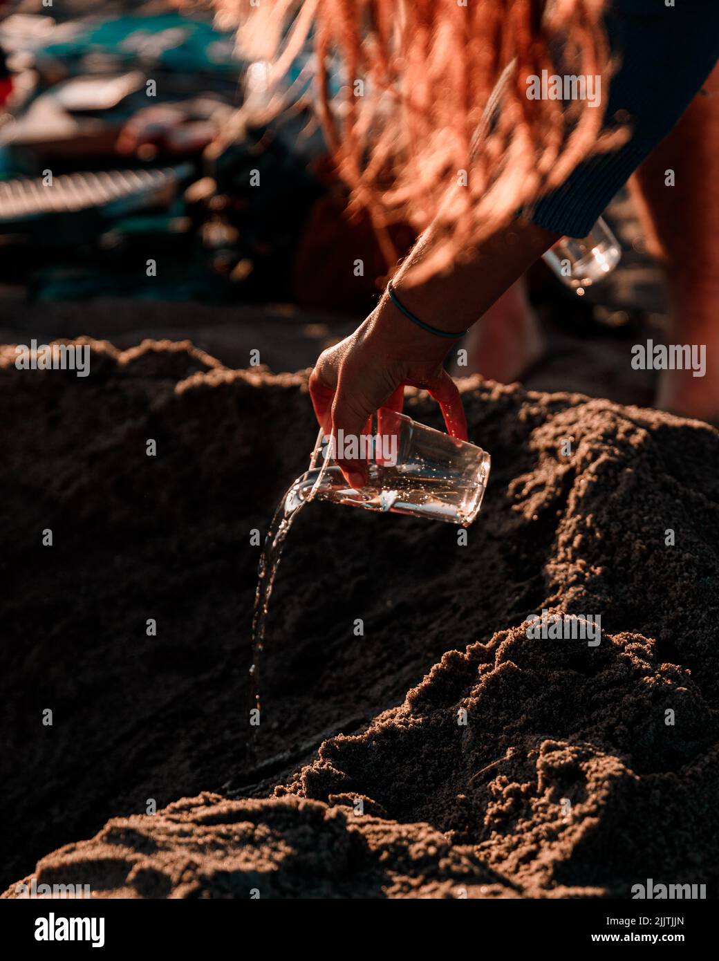 A woman pouring a water from glass cup on sands to build something on ...