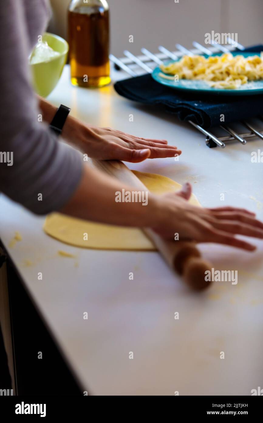 A vertical shot of a person rolling a dough with a rolling pin in the ...
