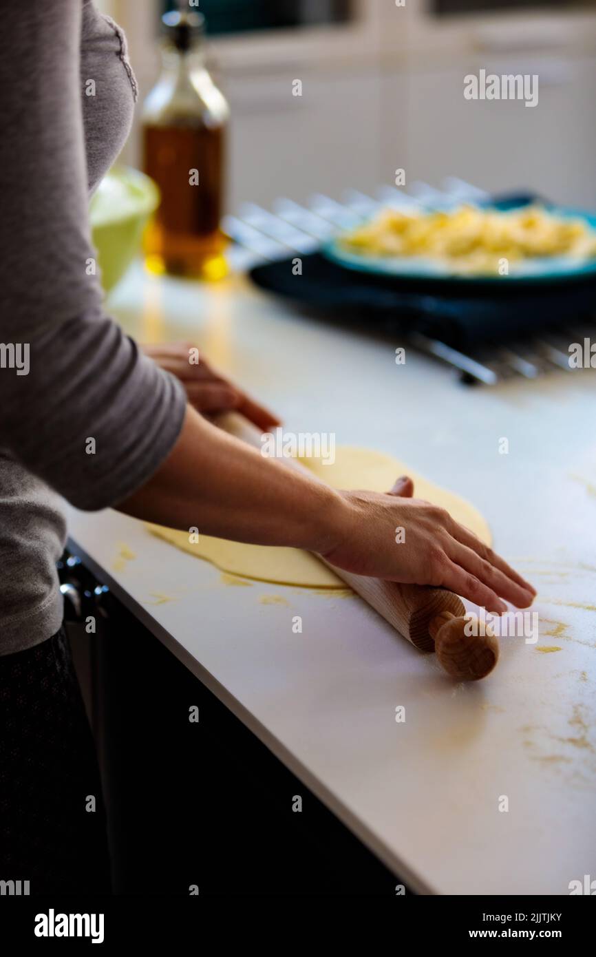 A vertical shot of a person rolling a dough with a rolling pin in the ...