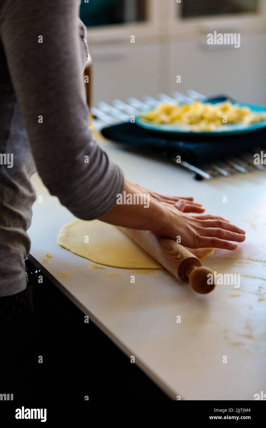 A vertical shot of a person rolling a dough with a rolling pin in the ...