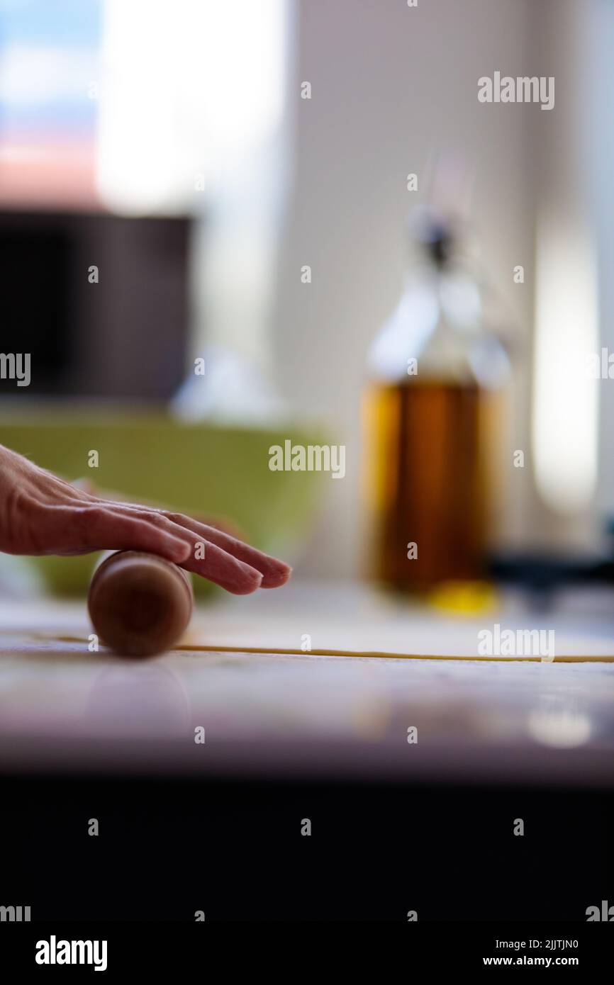 A vertical shot of a person rolling a dough with a rolling pin in the ...
