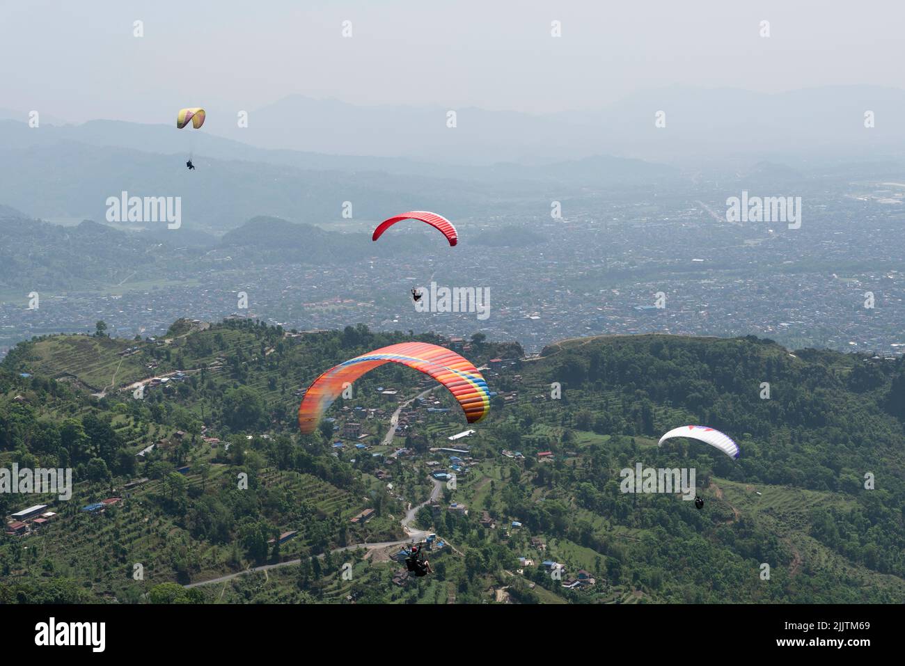 An aerial view of paragliders flying in the sky above the lush fields ...