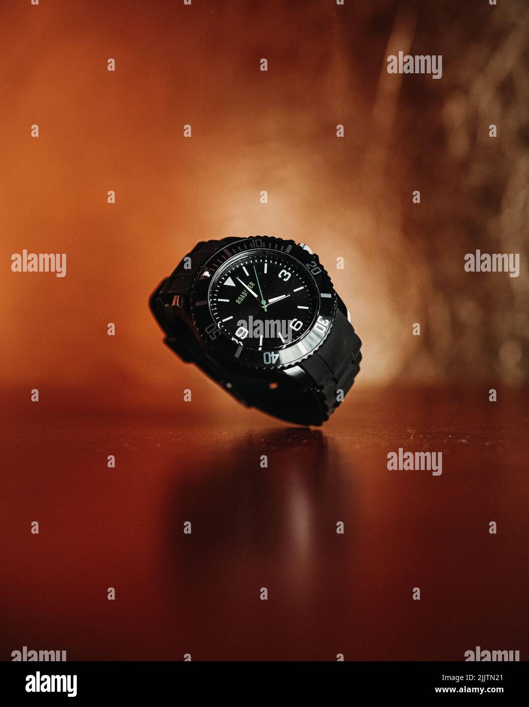 A vertical shot of a black hand watch on an orange-gold background ...