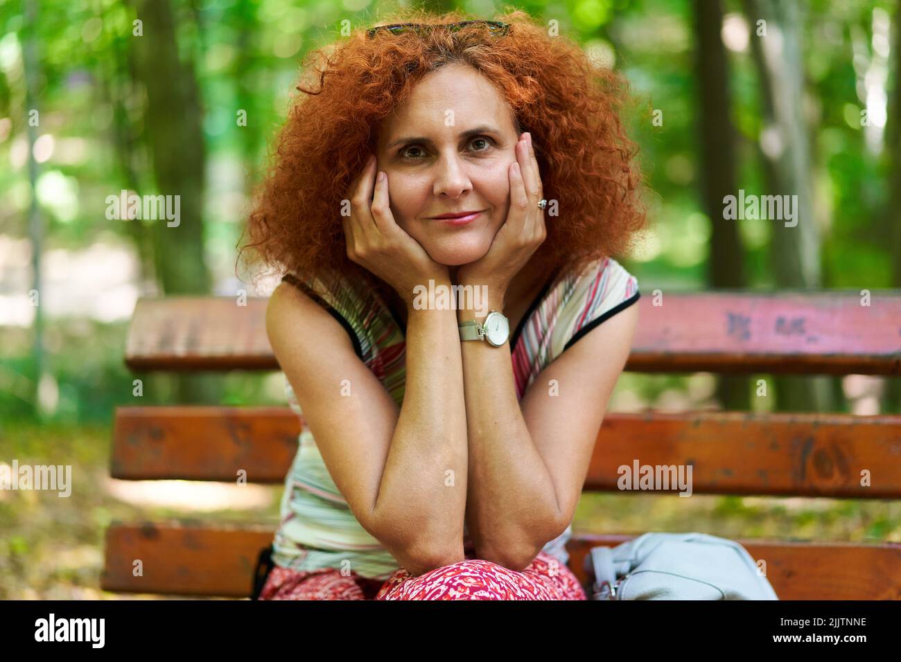 Redhead curly hair woman sitting on a bench in the park Stock Photo - Alamy
