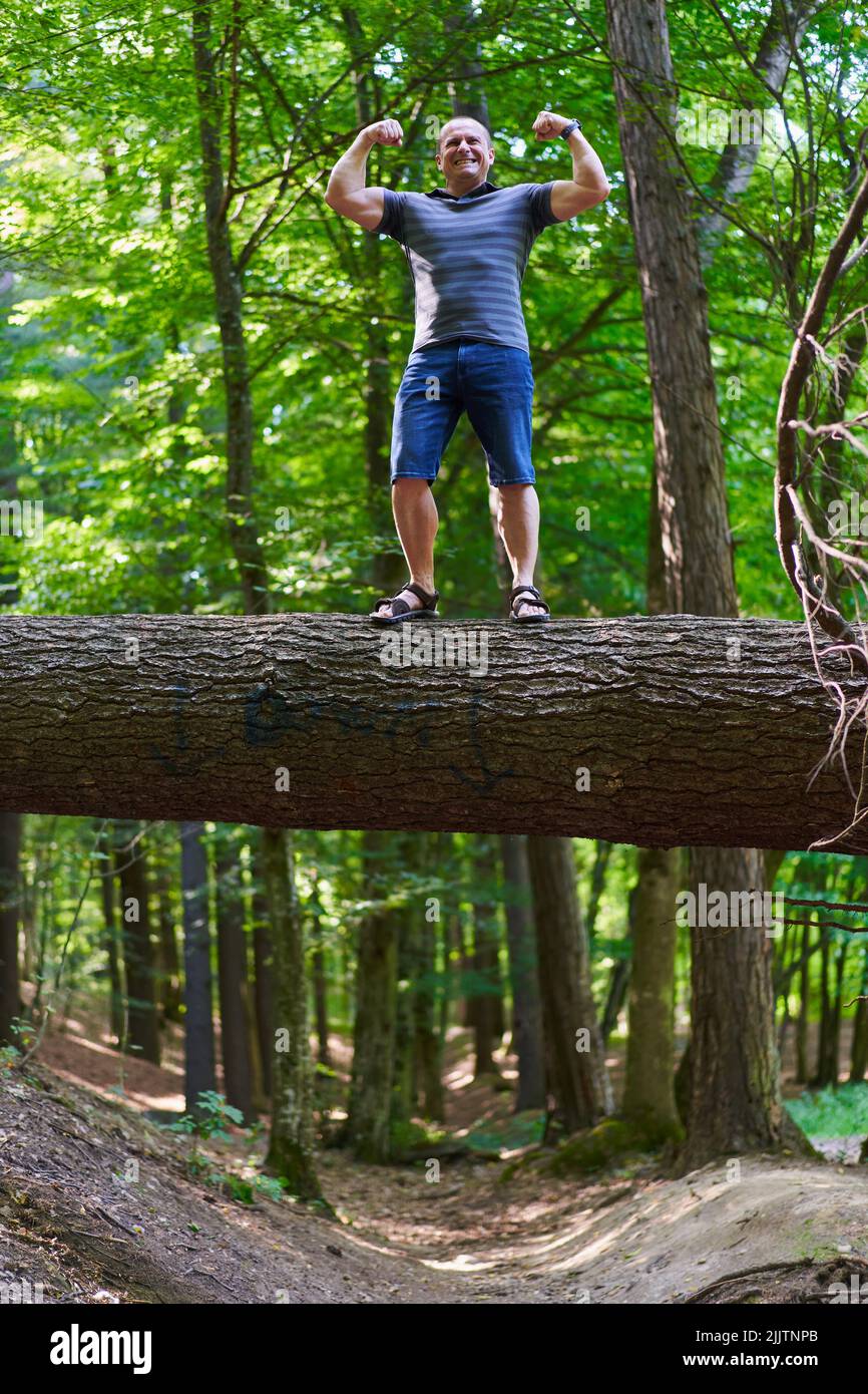 Strong athletic man climbing on a tree bark over a trail flexing his ...