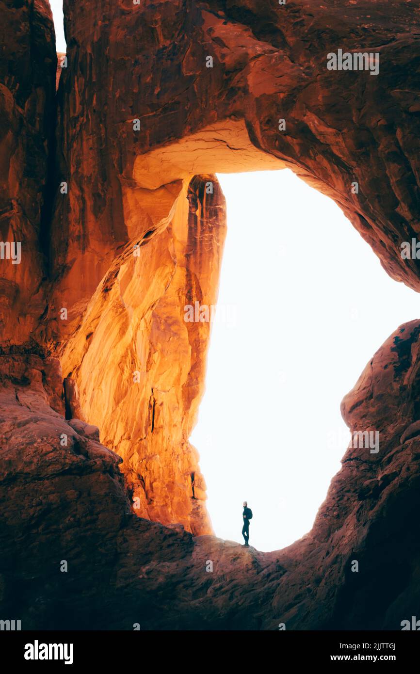 A vertical shot of a person standing under a rocky arch in the Grand ...