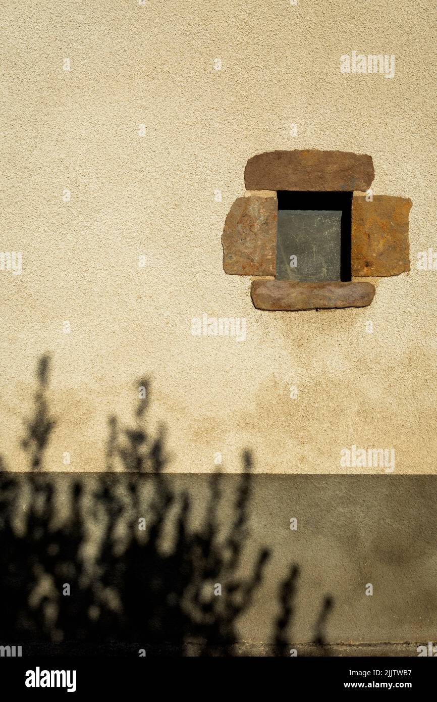 A vertical shot of a small square window on a beige wall with the ...