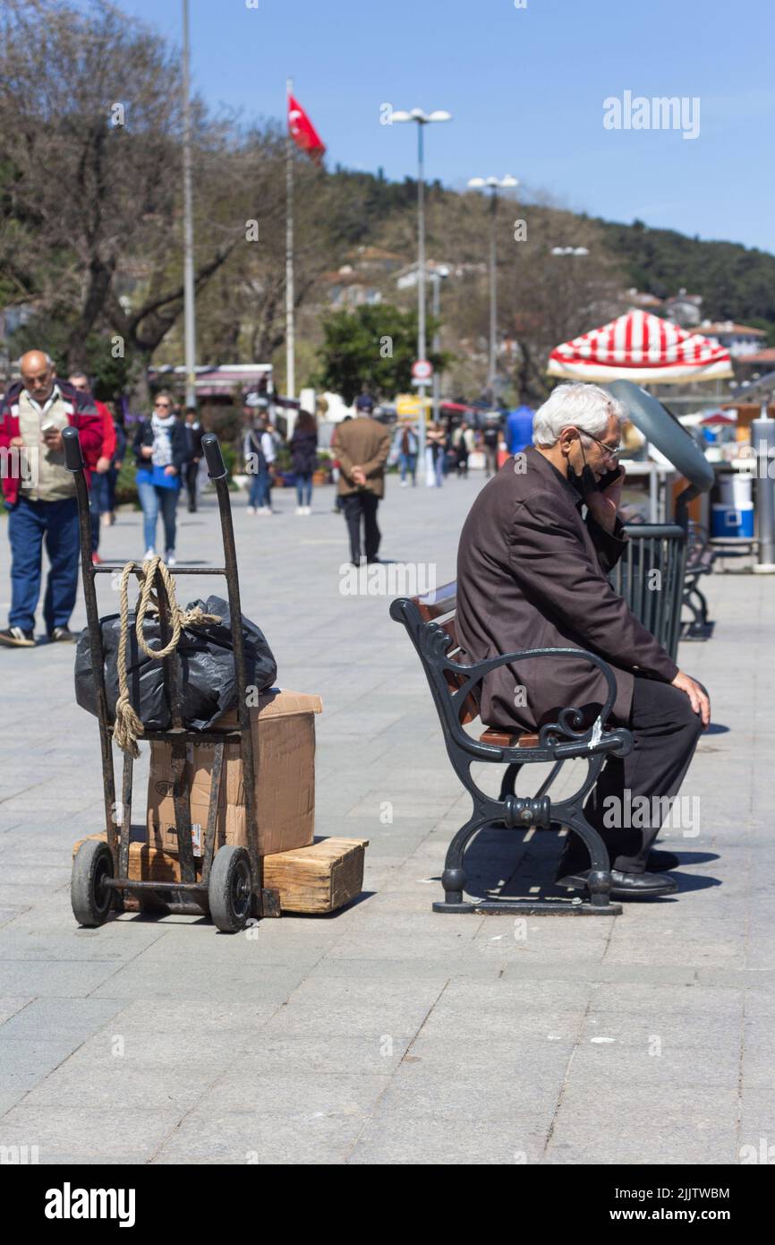 A vertical shot of an old man sitting on a bench while working and ...