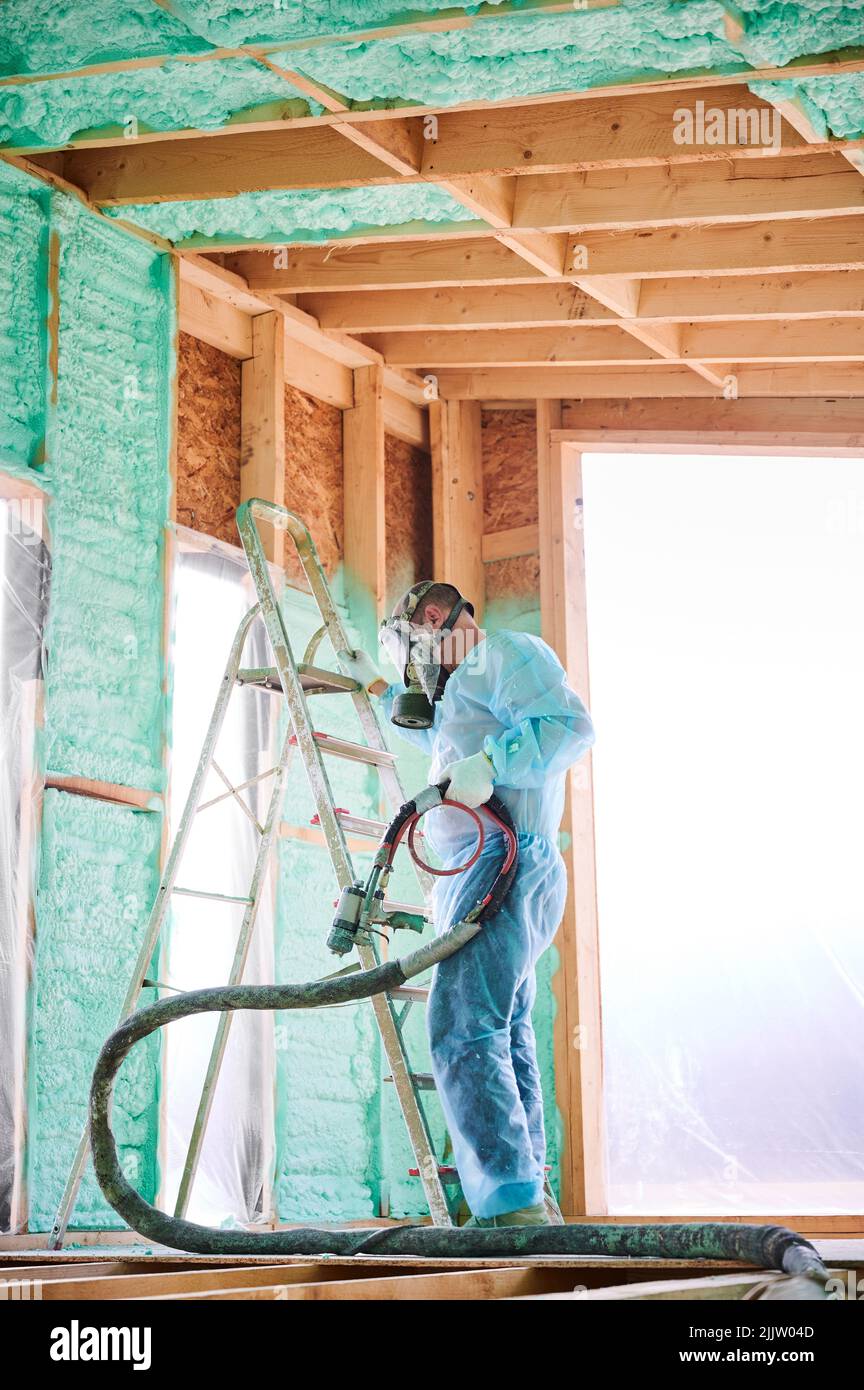 Male builder insulating wooden frame house. Man worker spraying ...