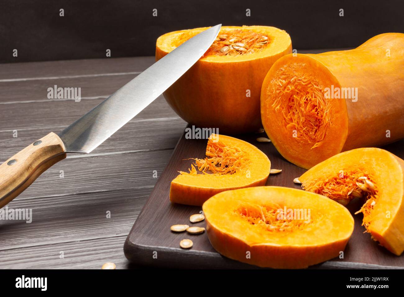 Pumpkin slices on stone cutting board. Knife on pumpkin. Top view. Dark ...