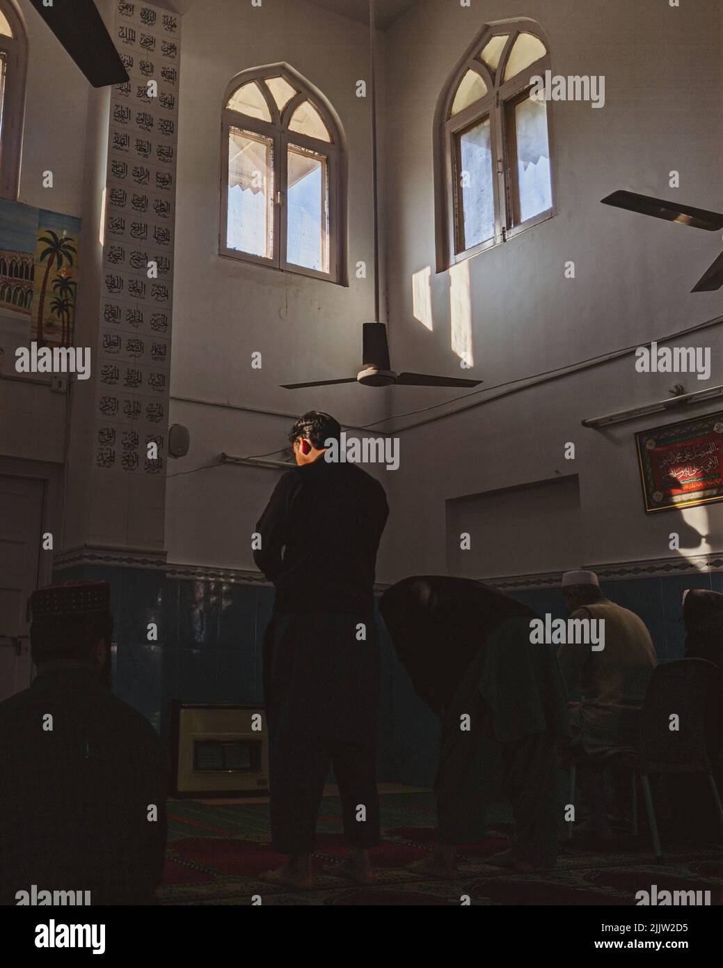 A vertical back view of a male worshipper praying in the Masjid Ashra ...