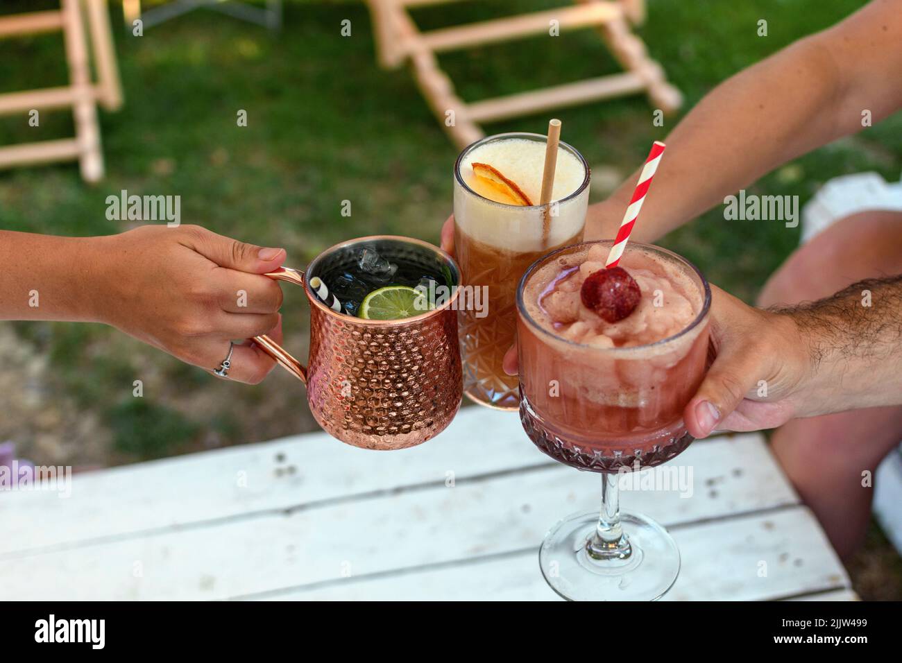 Three friends cheering with colorful cocktails outdoors Stock Photo - Alamy