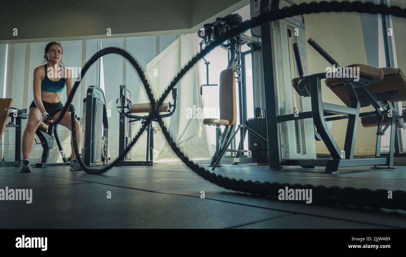 A low angle shot of an Asian woman doing battle rope exercise in the ...