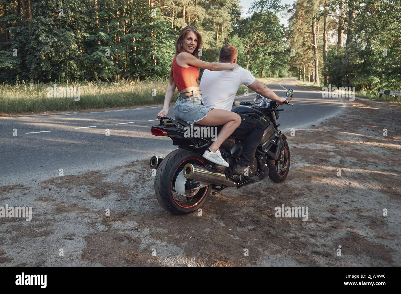 A young happy couple rides a motorcycle on an asphalt road in the ...