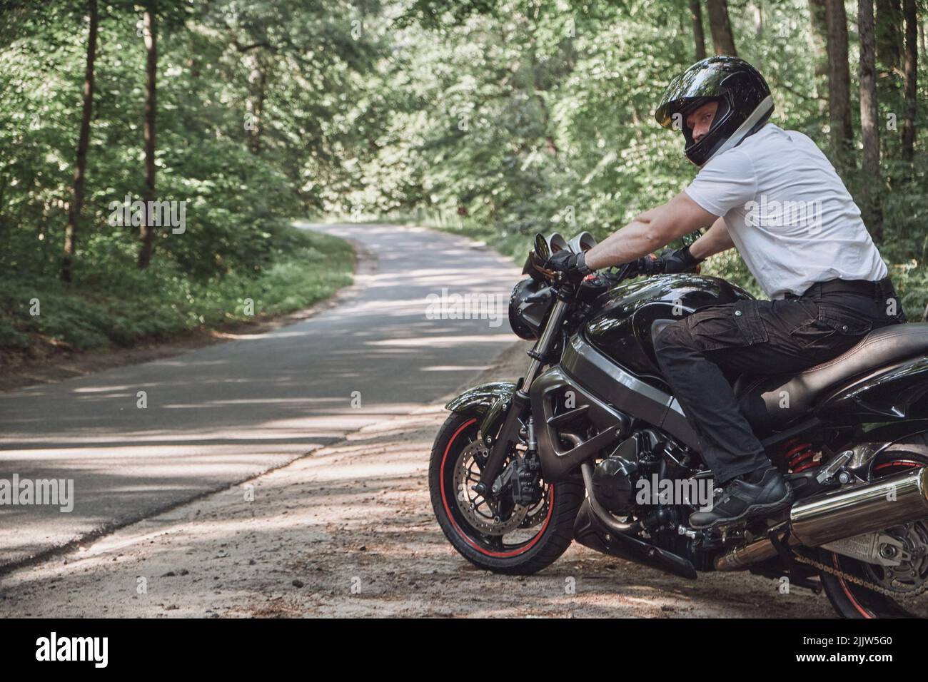 Young male biker in a helmet travels on a motorcycle alone, on a road ...