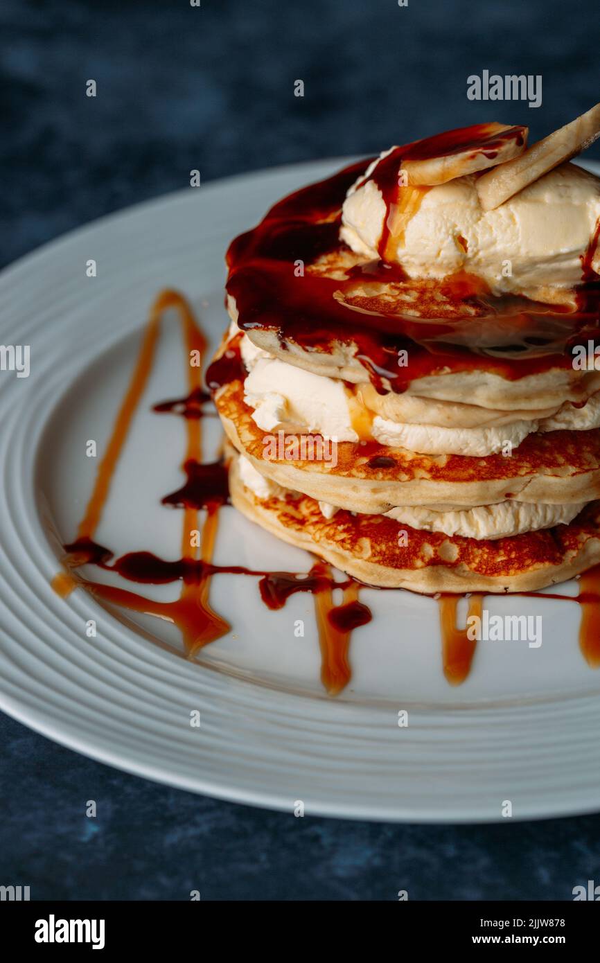 A vertical shot of pancakes with cream and bananas on a white plate ...