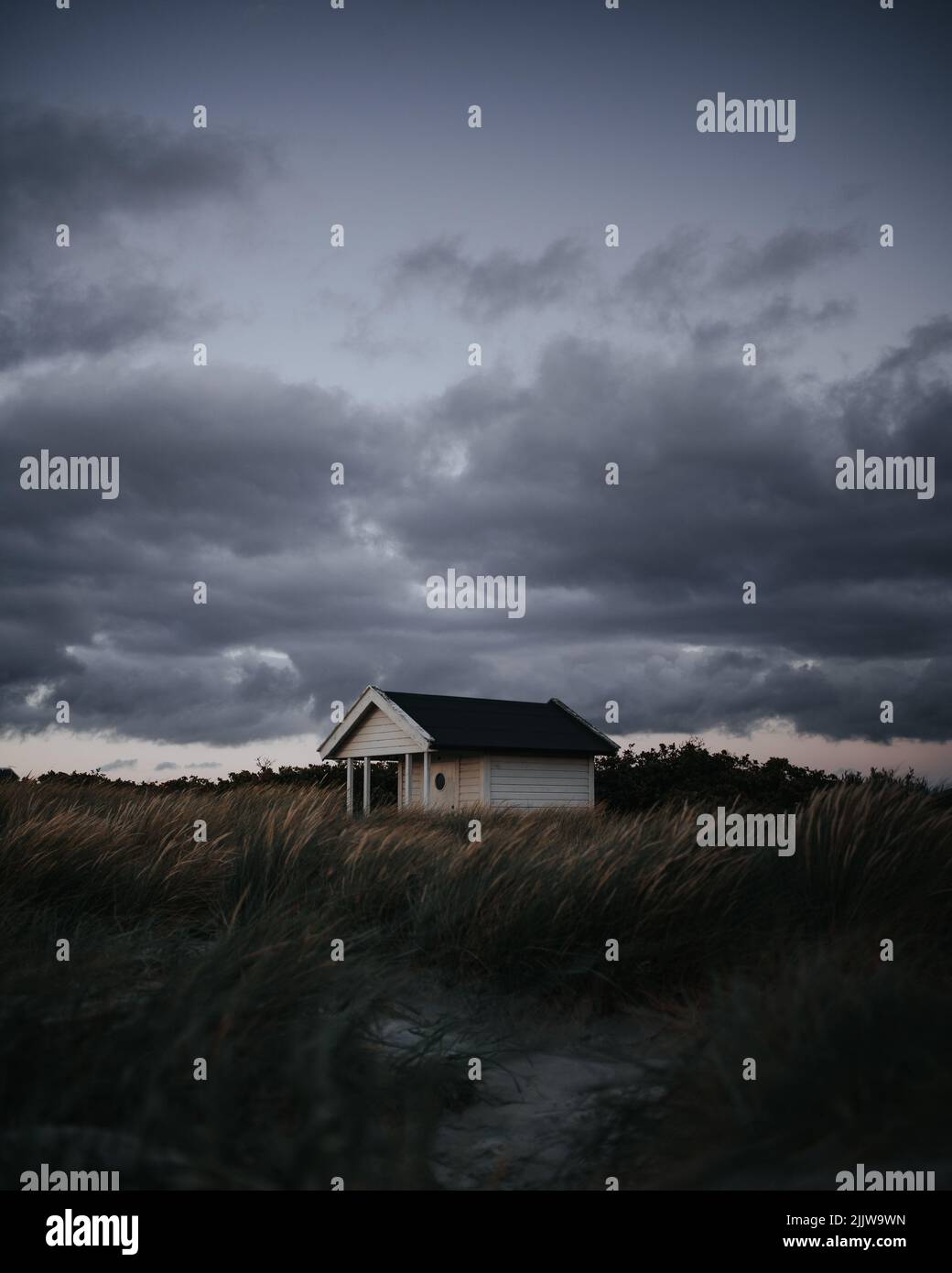 A vertical shot of a small house in the field with a cloudy sky in ...