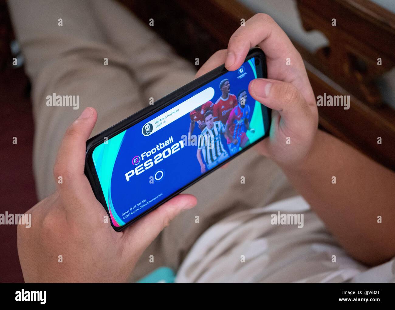 A closeup of a man using a mobile phone playing game PES 2021 at home ...