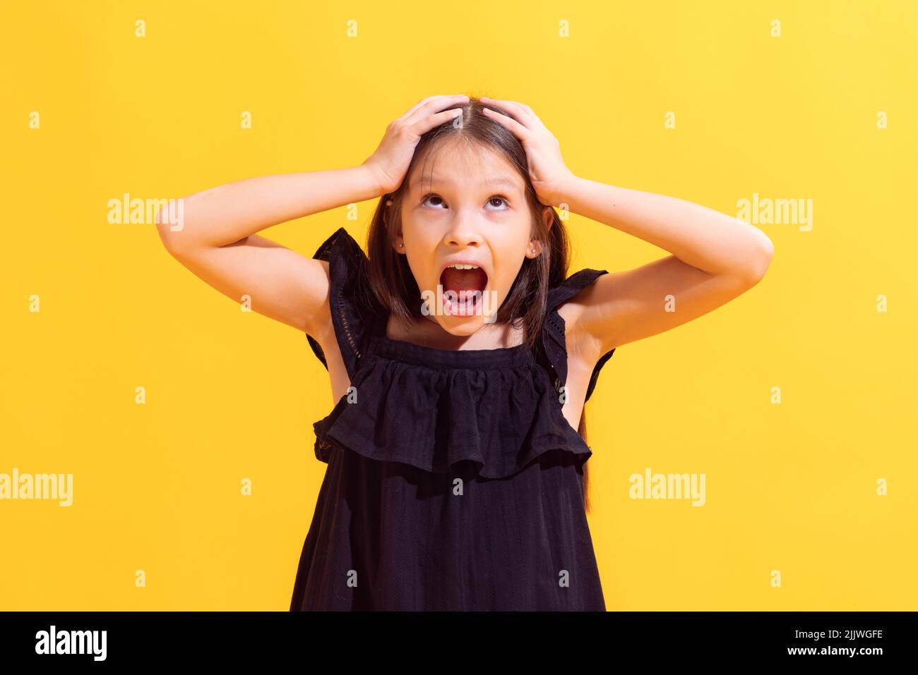 Shouting little girl, kid wearing black dress isolated on yellow ...