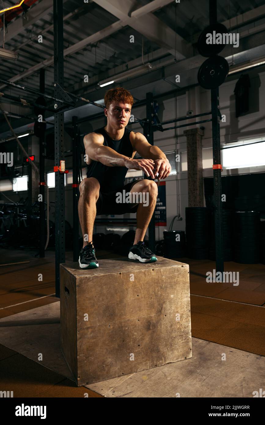 Portrait of sportive, muscular red-haired young man jumping on box ...