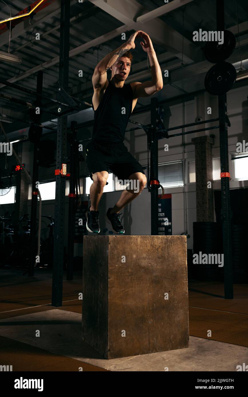 Portrait of sportive, muscular red-haired young man jumping on box ...