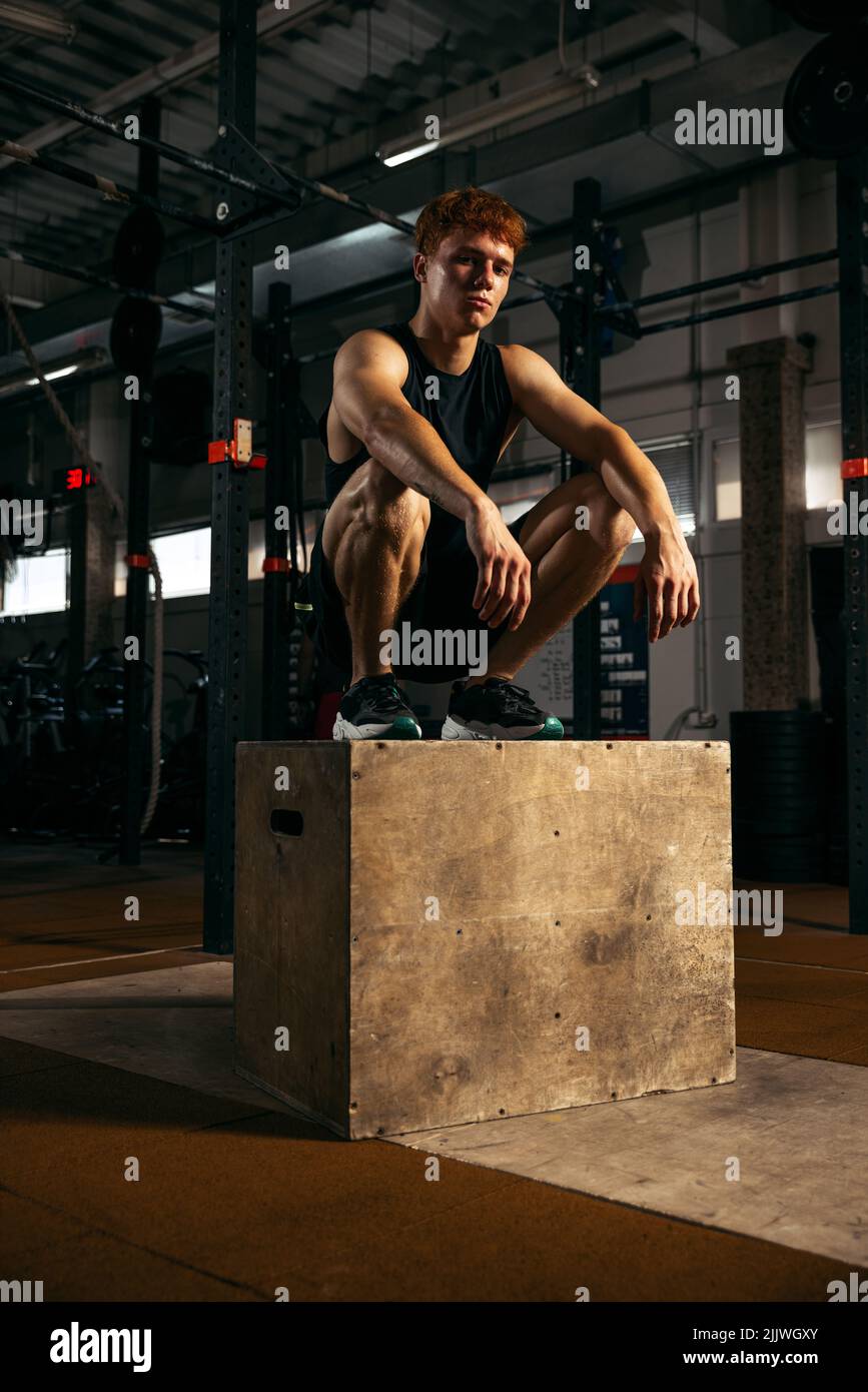 Portrait of sportive, muscular red-haired young man sitting on box ...