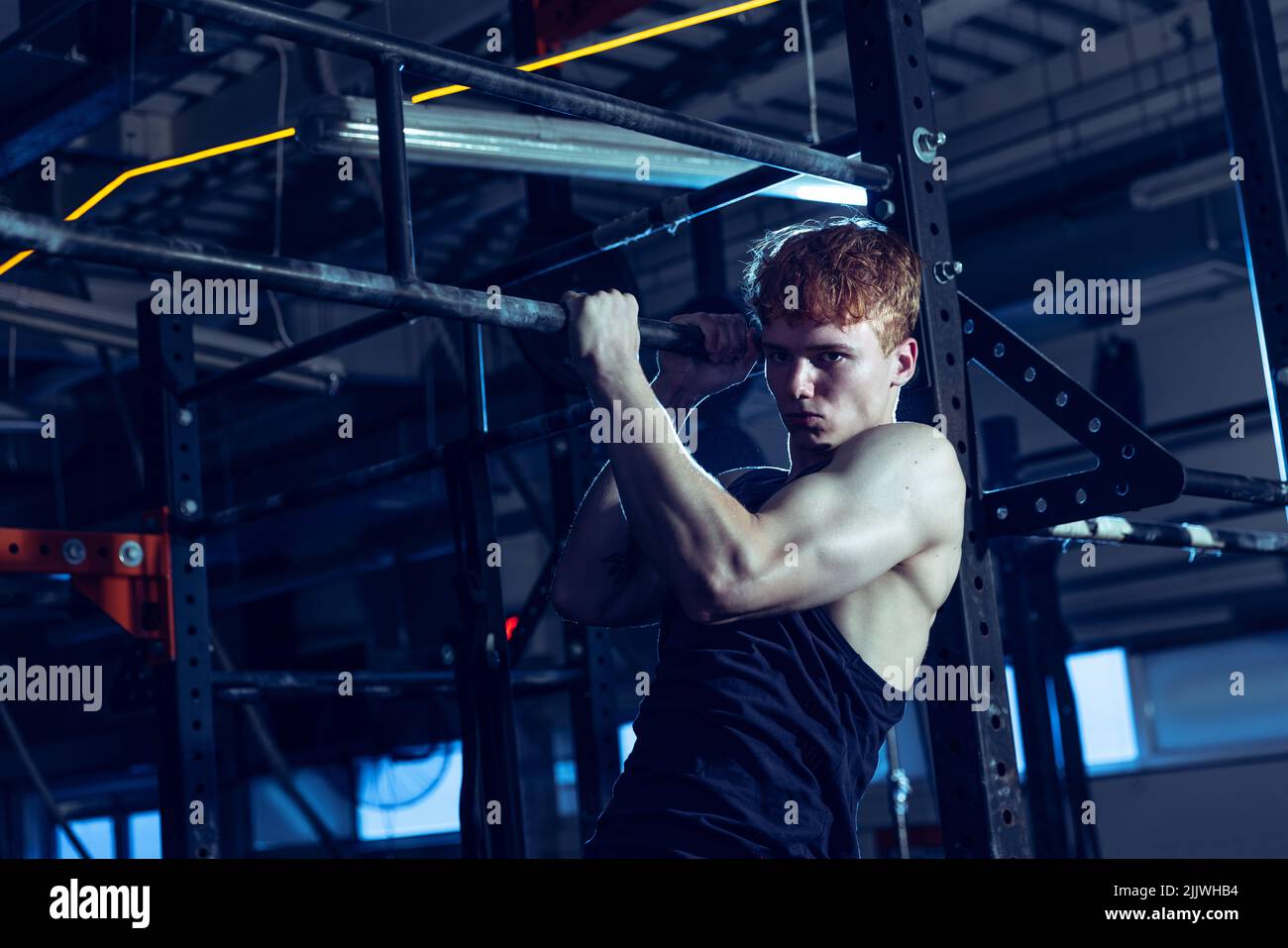 Portrait of sportive muscular young man training, doing pull up ...