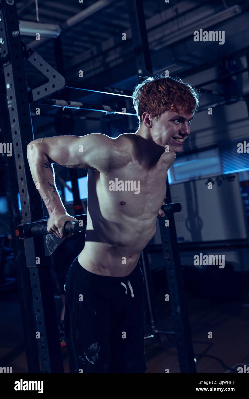 Portrait of young muscular man training, doing pull up exercises ...