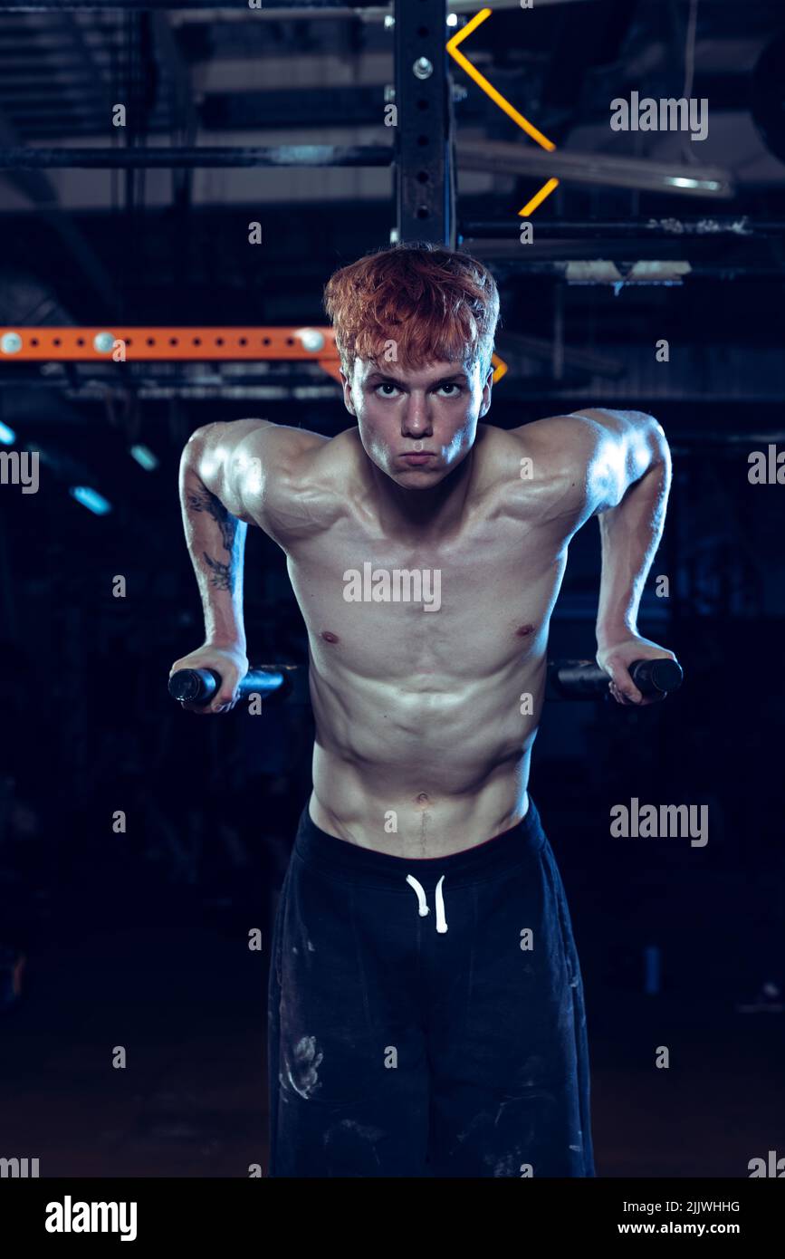 Portrait of young muscular man training, doing pull up exercises ...