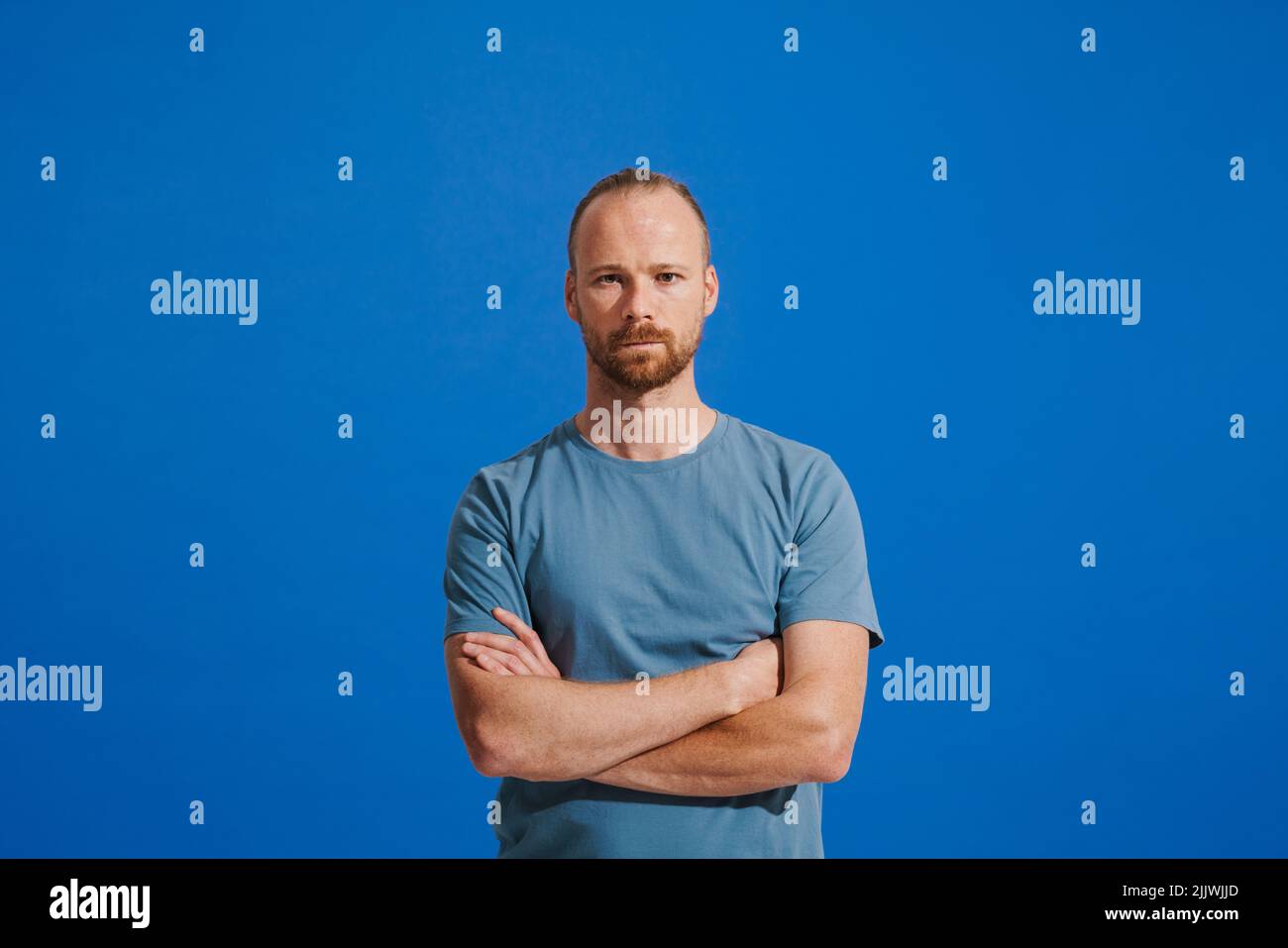 Ginger white man with beard posing with arms crossed isolated over blue ...