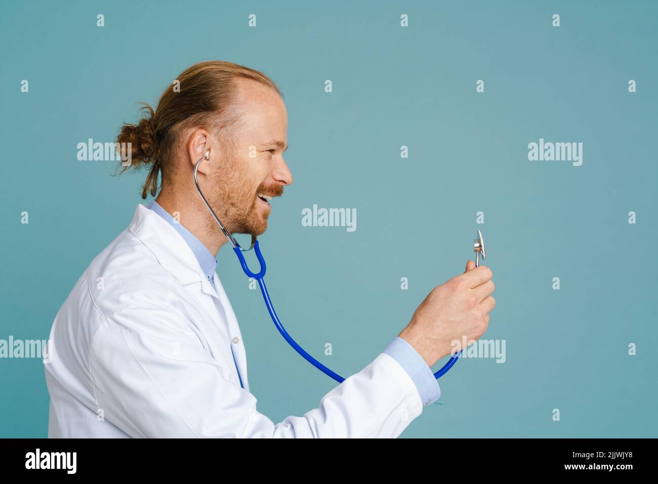 White male doctor wearing lab coat smiling and using stethoscope ...