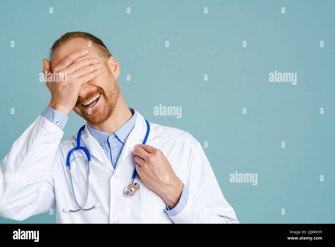 White male doctor wearing lab coat covering his eyes and laughing ...