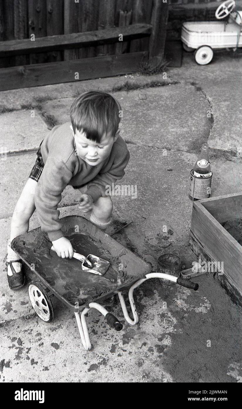 1960s, historical, outside on a patio, a small boy pating down the ...