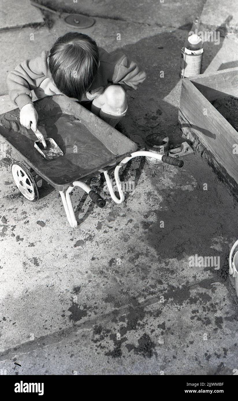 1960s, historical, outside on a patio, a small boy pating down the ...