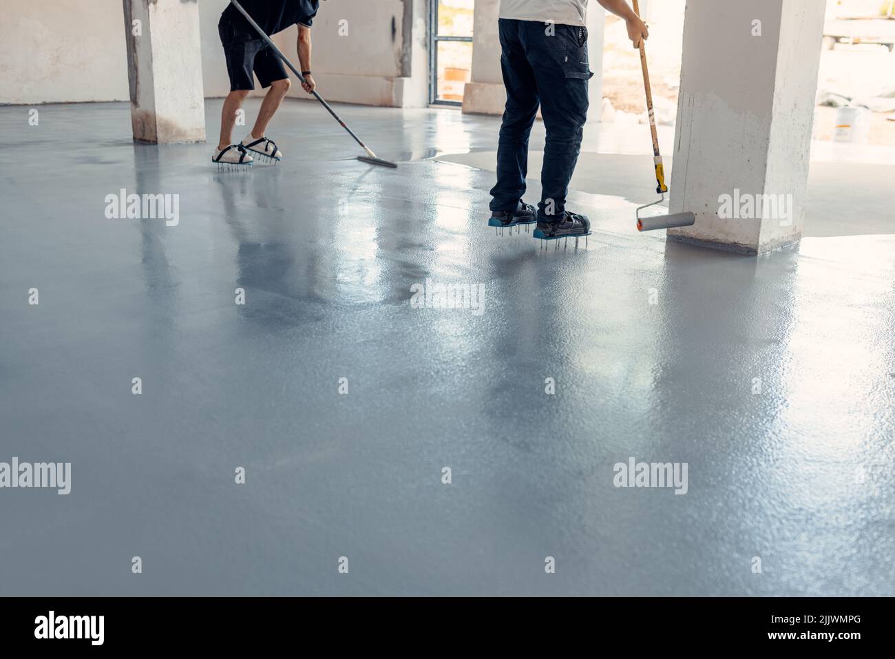 Two construction workers applying grey epoxy resin in an industrial ...