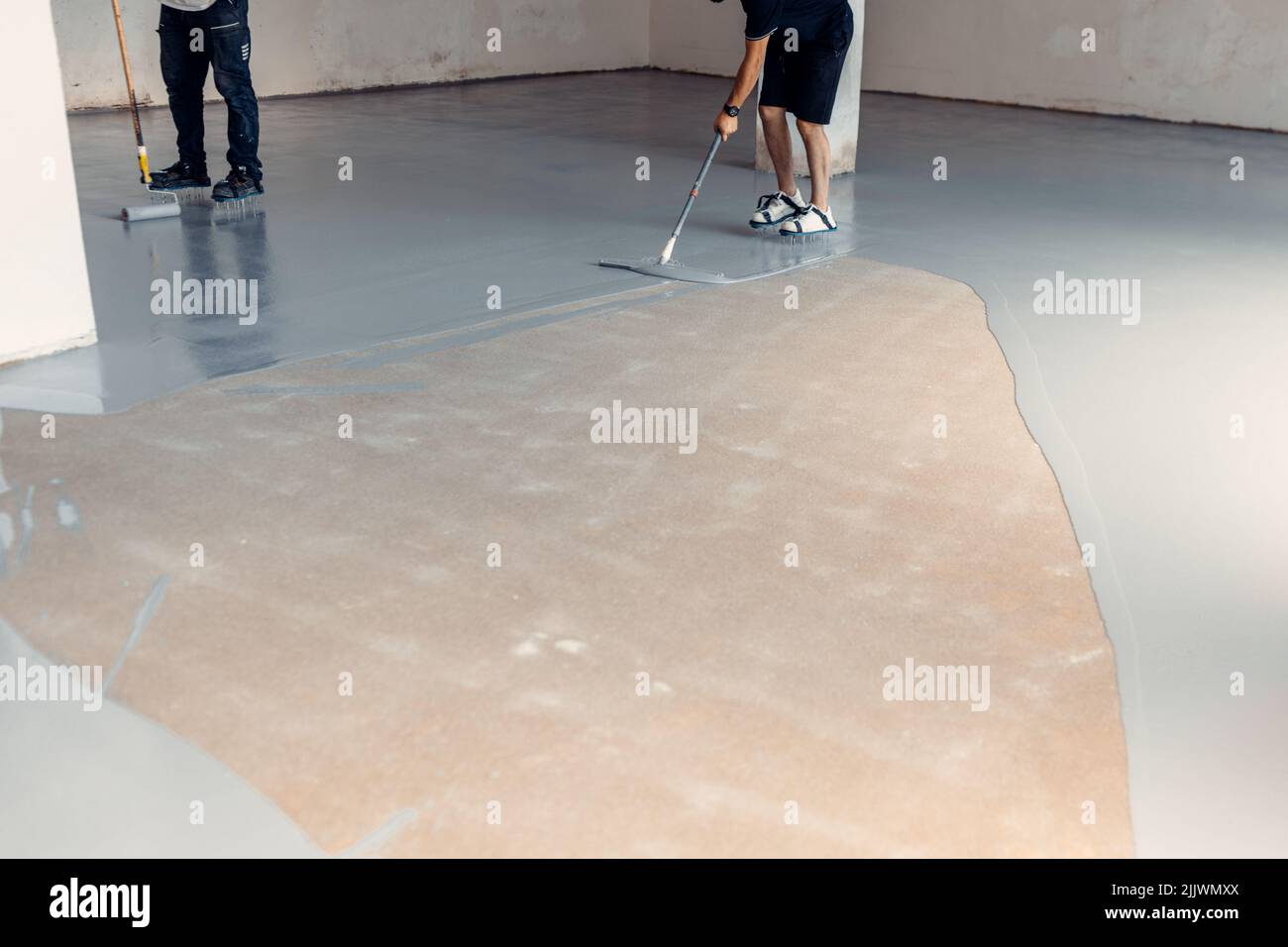 Two construction workers applying grey epoxy resin in an industrial ...