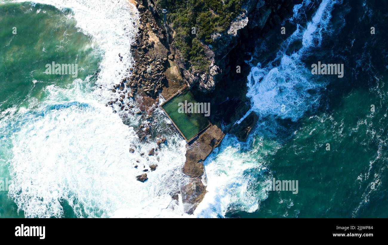 An aerial view of a blue wavy ocean and a cliffy shore during a daytime ...